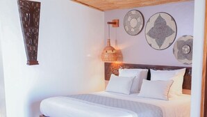 Uma cama bem arrumada com estrutura de madeira e roupa de cama branca, um tapete de parede tecido e três pratos decorativos na parede.