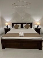 Uma cama grande com estrutura de madeira, duas mesas de cabeceira com abajures e um detalhe decorativo no teto.