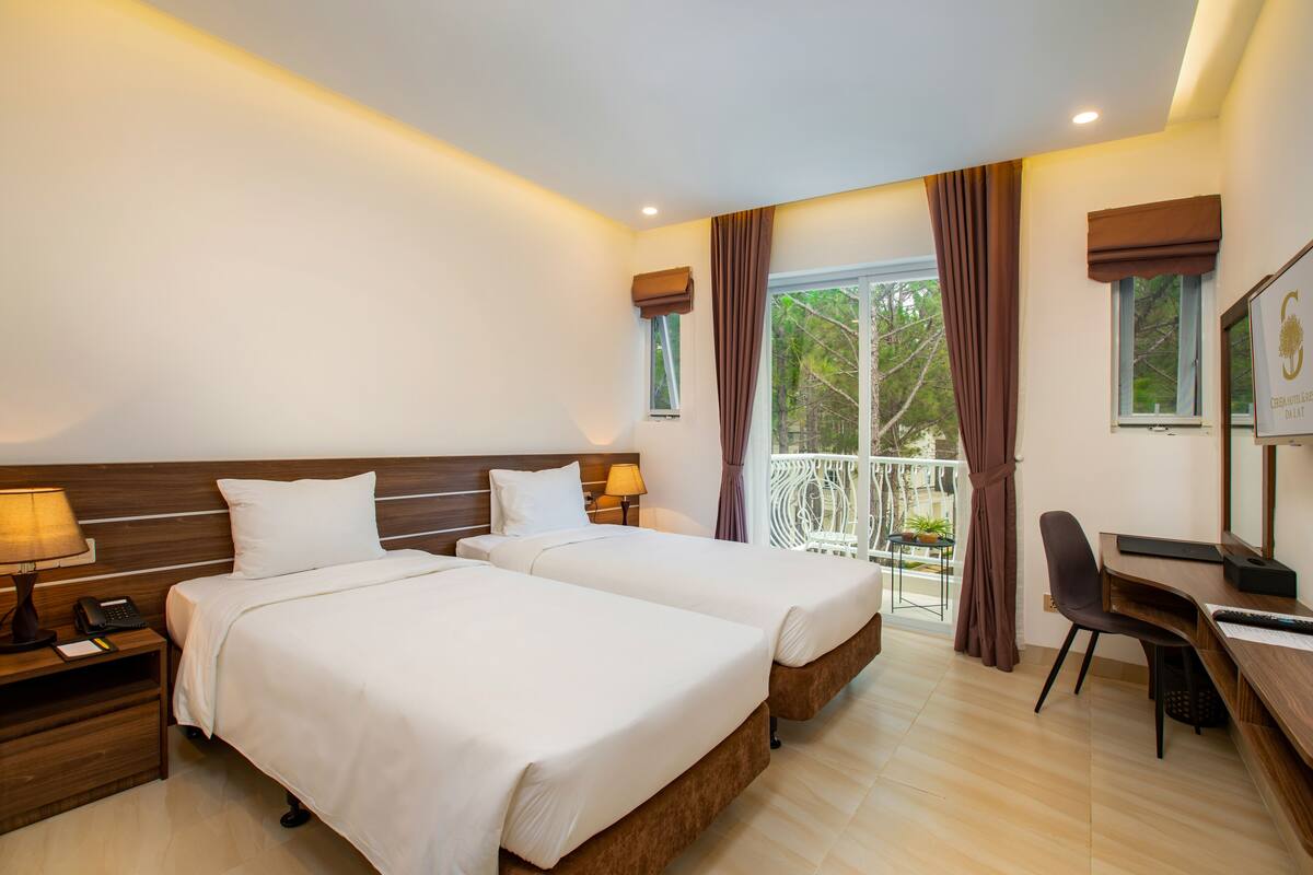 Quarto de hotel com duas camas, uma escrivaninha e varanda com guarda-corrimão.