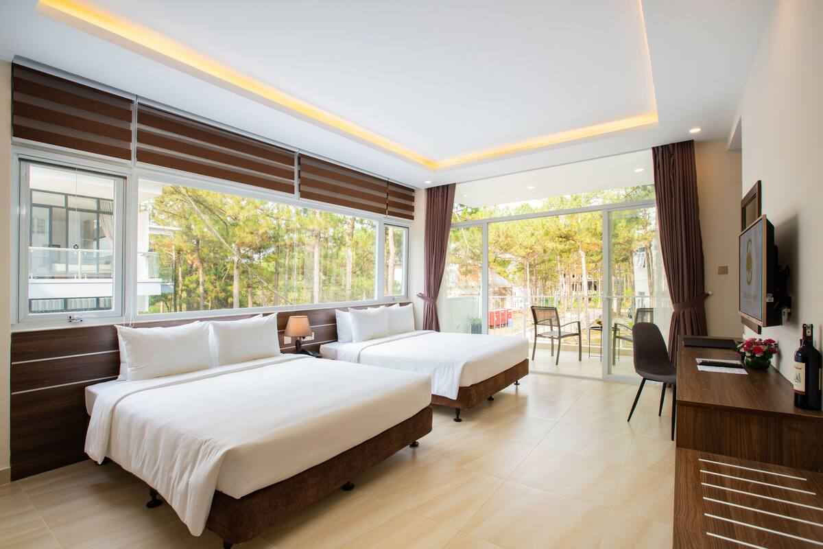 Quarto de hotel com duas camas, uma escrivaninha e vista para o exterior.