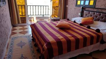 Quarto de hotel com uma cama grande, uma mesinha e vista para a varanda externa.