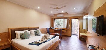 Quarto de hotel com cama, escrivaninha, cadeira e televisão.