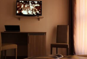 Quarto de hotel com televisão na parede, secretária com um laptop, cadeira e cama.