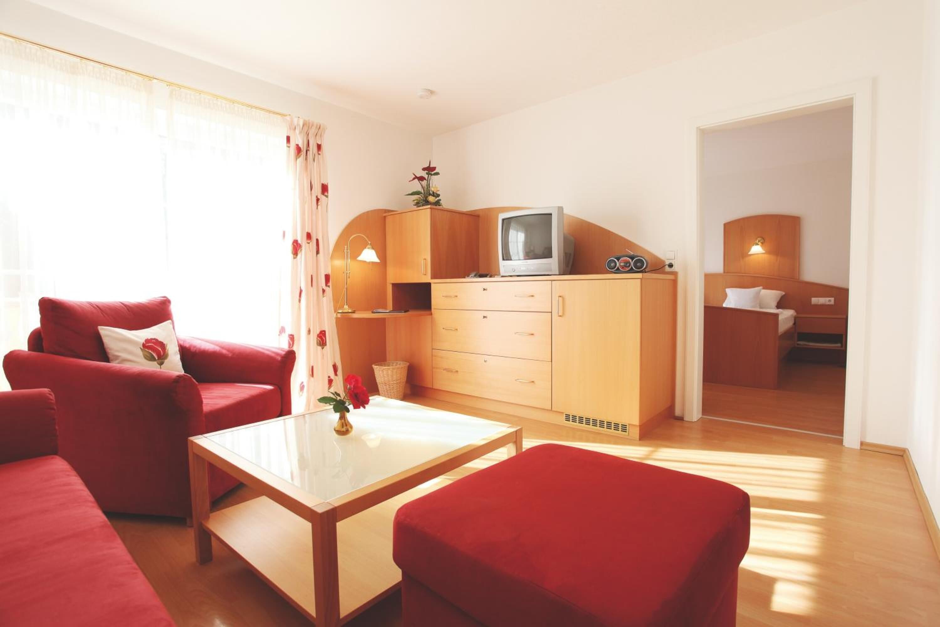 Um espaço compacto com cozinha americana, um sofá vermelho, uma mesa pequena e uma cama.