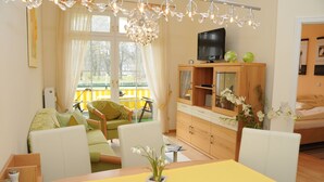Uma sala de estar acolhedora, com um sofá, cadeiras, um armário de madeira com uma TV e uma mesa de jantar com toalha amarela.