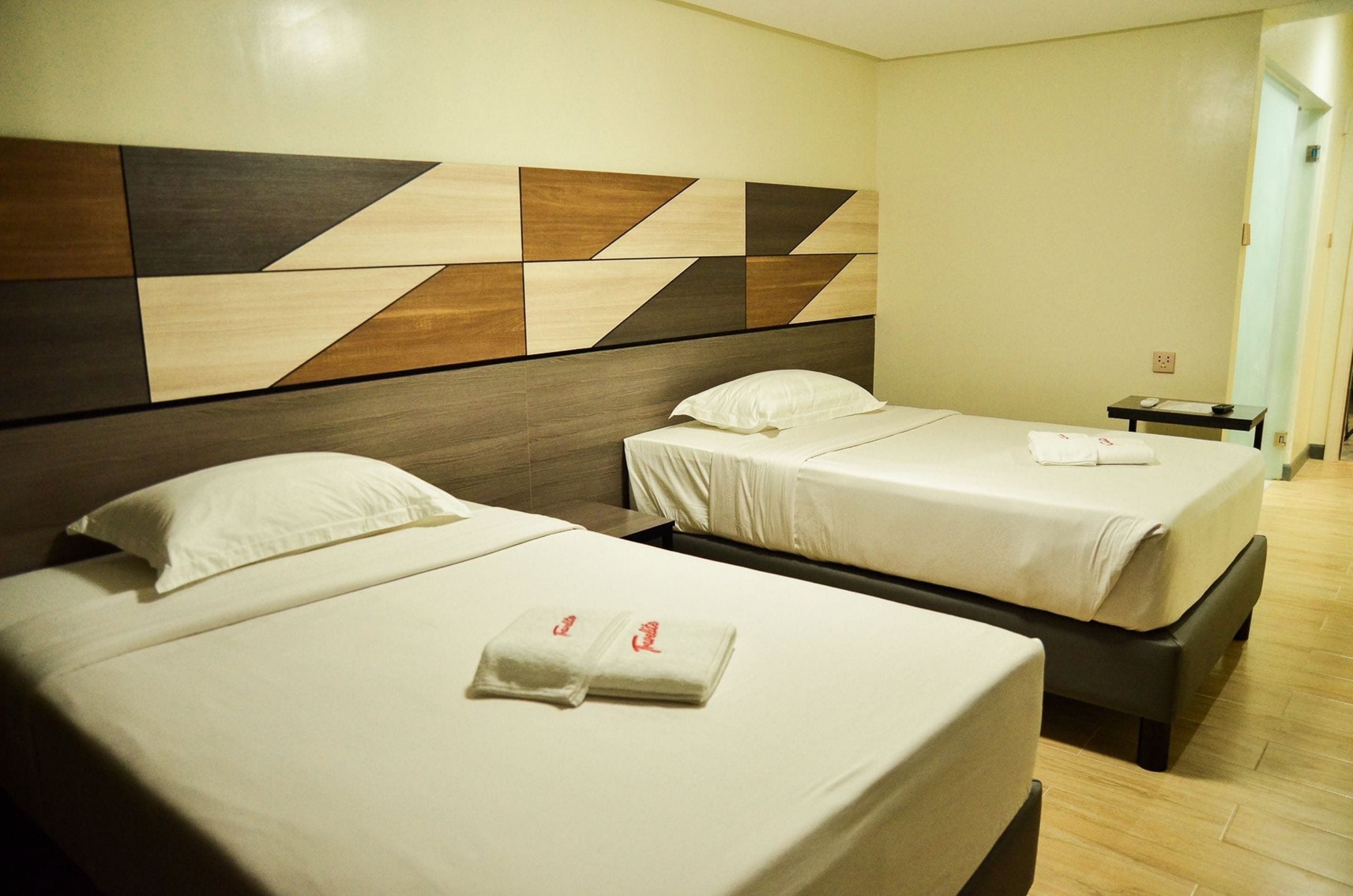 Quarto de hotel com duas camas, cada uma com travesseiro e toalha dobrada.