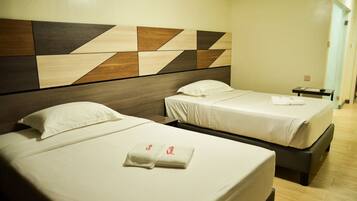 Quarto de hotel com duas camas, cada uma com travesseiro e toalha dobrada.