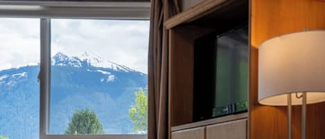 Quarto com janela que oferece vista para montanhas, um armário de madeira e uma luminária.
