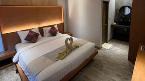 Quarto de hotel moderno com uma cama grande, cabeceira de madeira e arranjo de toalhas diferenciado na cama.