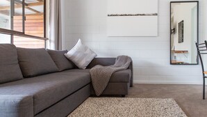 Uma sala de estar moderna com um sofá cinzento, um cobertor e um espelho grande na parede.