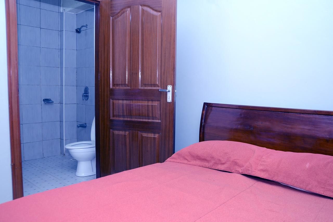 Quarto com cabeceira de madeira, colcha rosa e uma casa de banho pequena com azulejos e chuveiro.