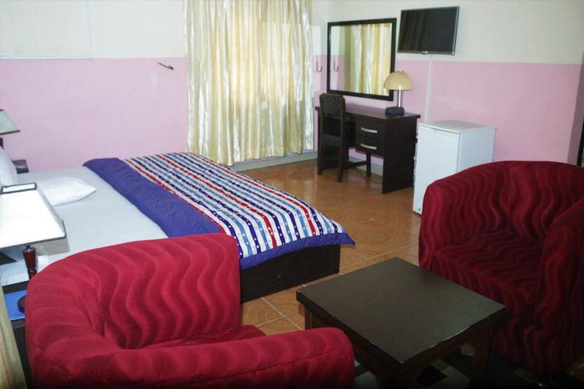 Quarto com cama, escrivaninha, cadeira, mesa, televisão e luminária.