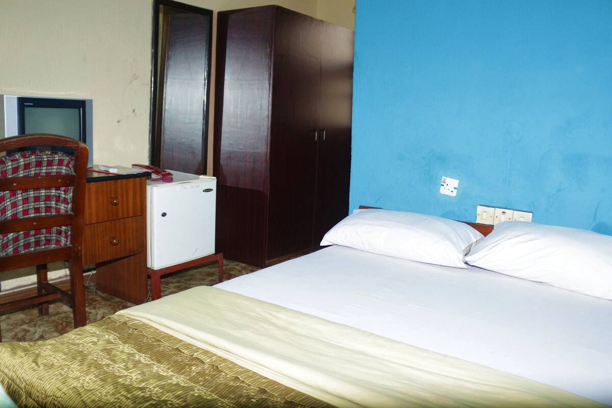 Quarto com cama, escrivaninha, guarda-roupa e televisão.