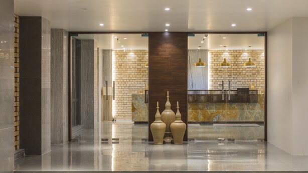 Um lobby moderno com divisória de vidro, balcão de recepção e vasos decorativos.
