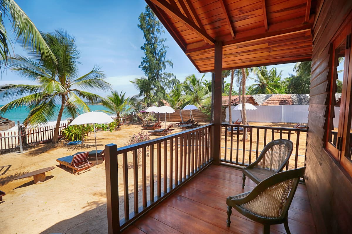 Um deck de madeira com vista para uma praia arenosa e palmeiras.