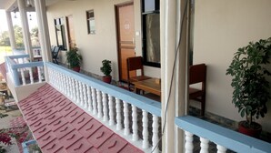 Varanda coberta com guarda-corpo vermelho e azul, plantas em vasos e mesa de madeira com cadeiras.
