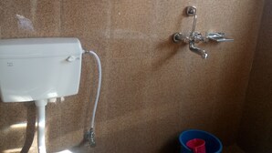 Casa de banho com sanita, chuveiro e um balde azul no chão.