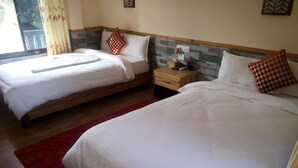 Quarto de hotel com duas camas, um tapete vermelho, uma mesinha de cabeceira com controle remoto e uma janela com cortinas.