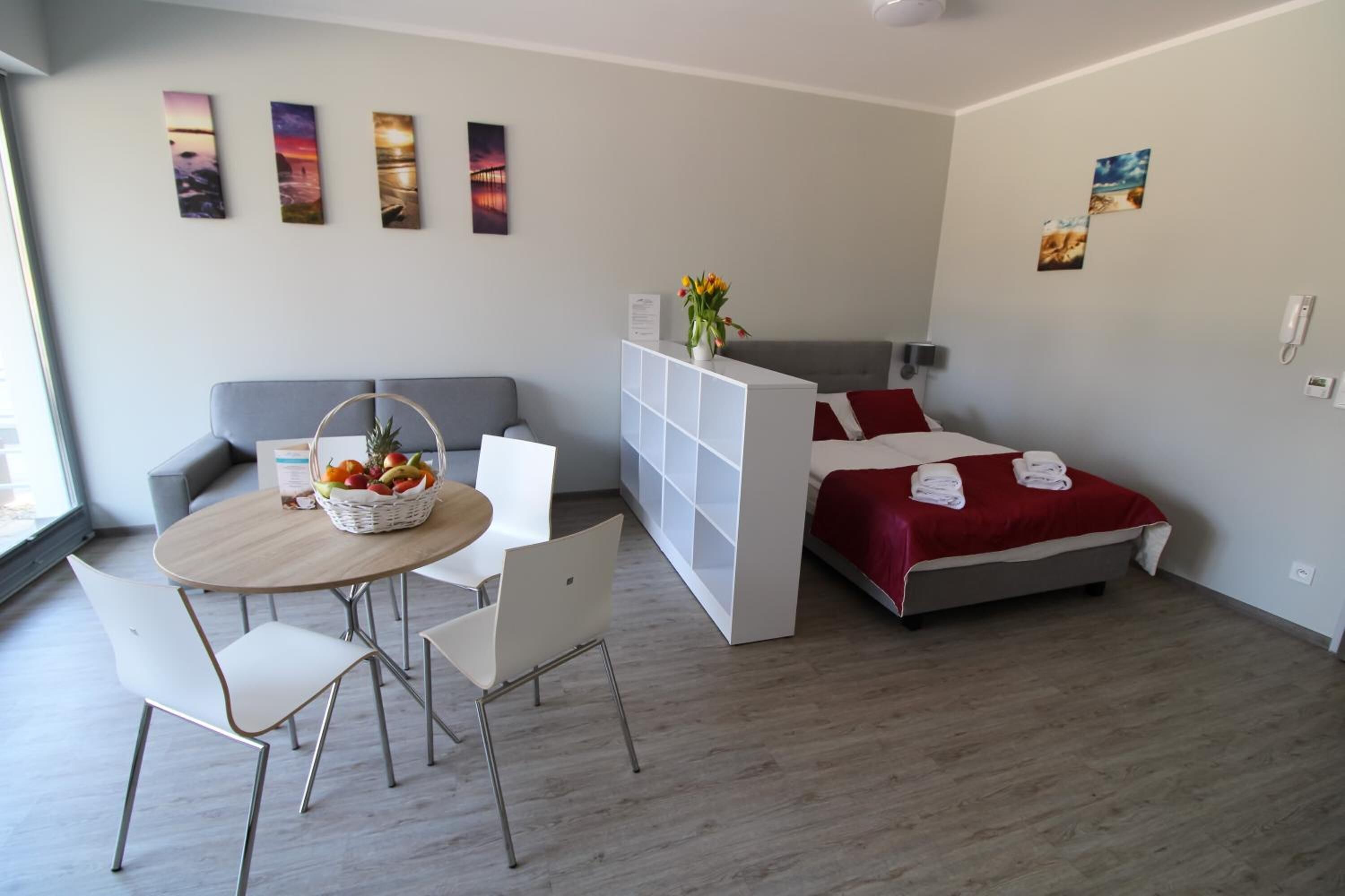 Quarto de hotel moderno com uma cama, um espaço de estar com uma mesa e cadeiras, um armário pequeno branco e obras de arte nas paredes.
