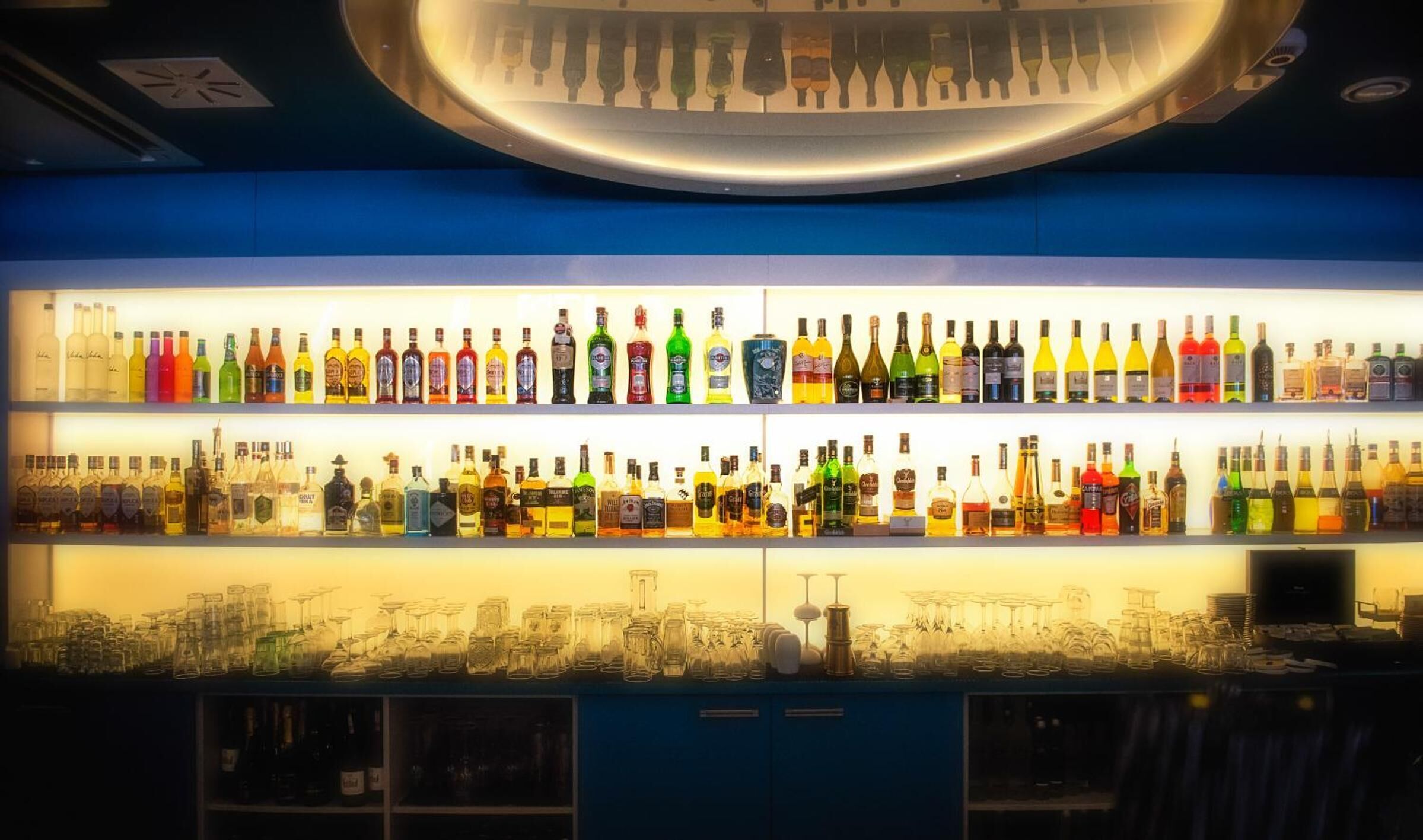 Um bar com várias prateleiras cheias de garrafas de bebidas e uma grande variedade de copos de vinho no balcão.
