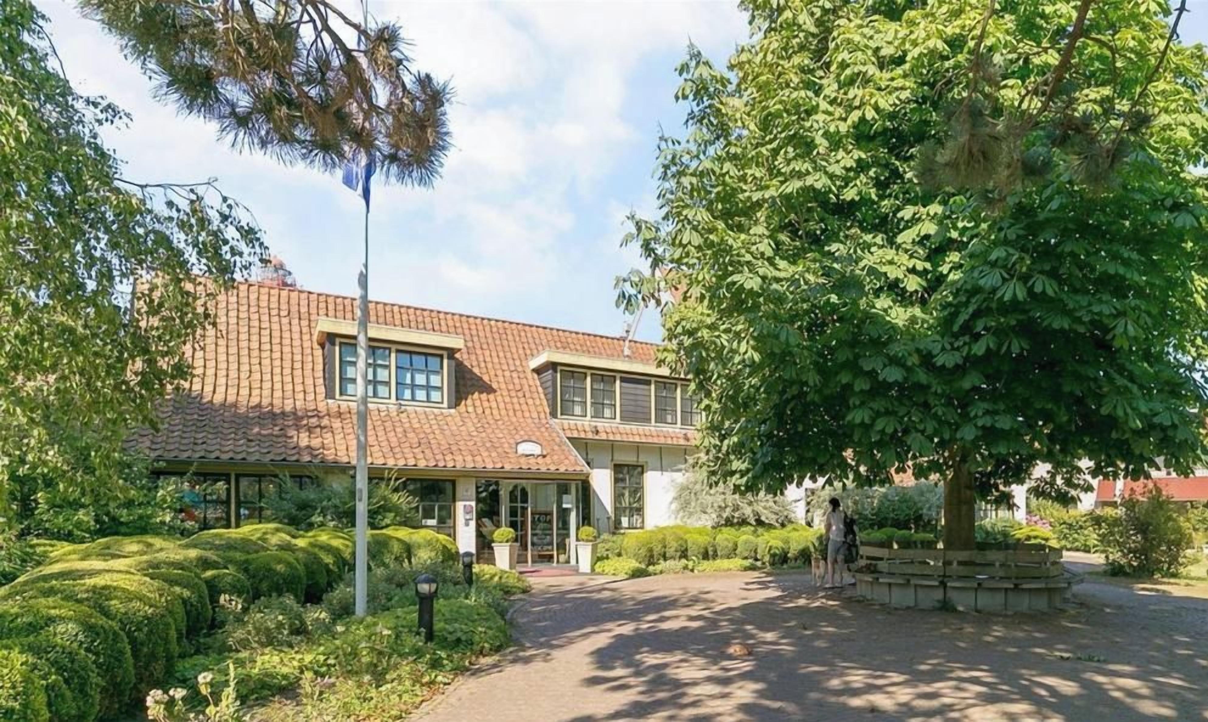 Um edifício com telhado de azulejos, rodeado por jardins bem cuidados e uma grande árvore.