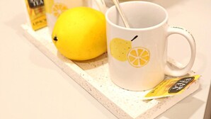 Uma bandeja com duas canecas brancas decoradas com limões, um limão e um recipiente de vidro com limões e um ramo de folhagem.