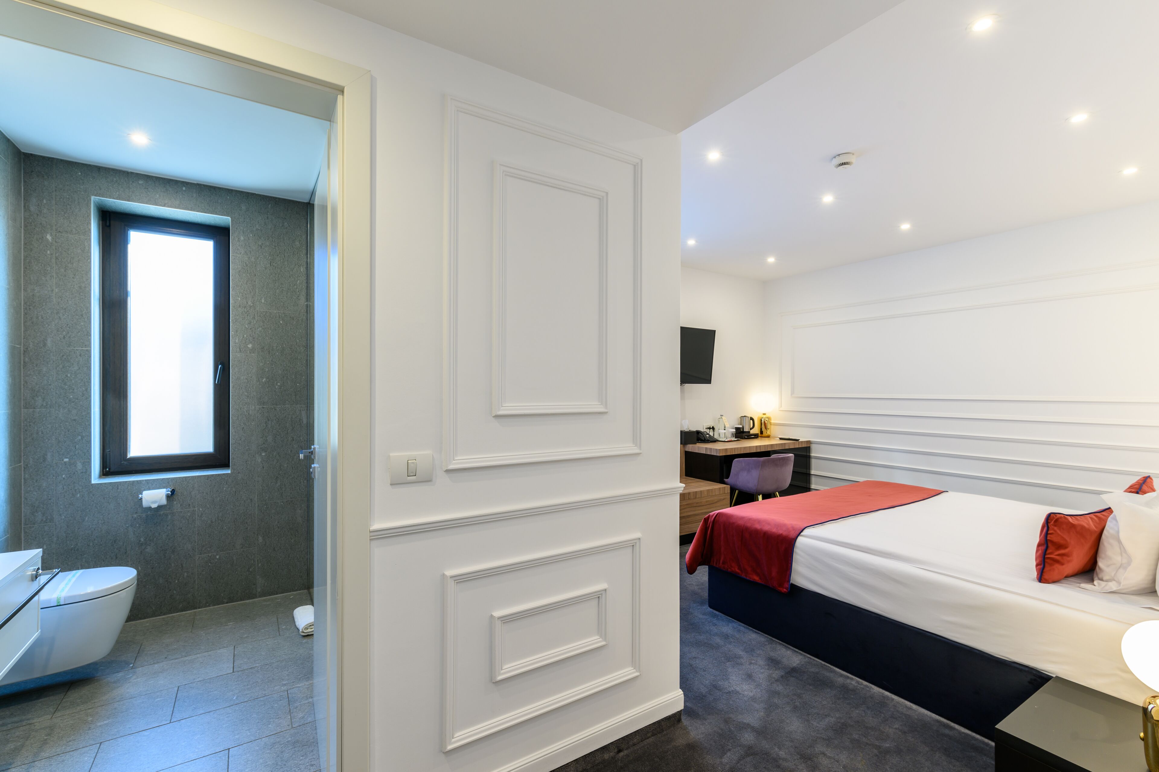 Quarto de hotel moderno com uma cama grande, uma escrivaninha e um banheiro com chuveiro e vaso sanitário.