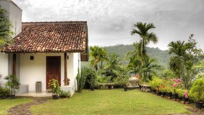 Uma casa com telhado de telhas, porta frontal e um pequeno jardim com diversas plantas e um caminho.