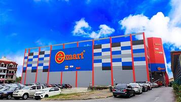 Um edifício grande com um letreiro chamativo 'eMart', cercado por carros estacionados e um céu azul límpido.