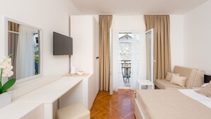 Quarto de hotel moderno com piso de madeira, cama, sofá, escrivaninha e televisão.