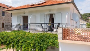Uma casa de dois andares com telhado de telhas vermelhas, paredes externas brancas e uma varanda com grade de metal.