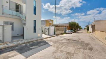 Rua residencial com casas modernas, céu claro e carros estacionados.
