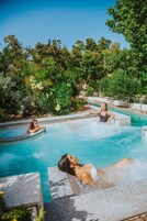 Uma área de piscina com água azul cristalina, rodeada por vegetação exuberante e árvores.