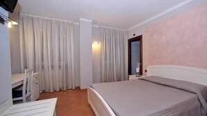 Quarto de hotel com cama, escrivaninha e cadeira.