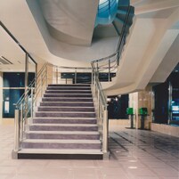 Interior moderno com escadaria sinuosa, guarda-corpos de metal e um poço de elevador em vidro.