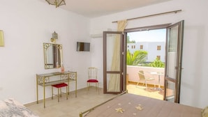 Quarto com cama, escrivaninha, cadeira, televisão e varanda com mesa e cadeiras.