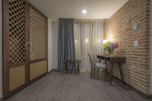 Um quarto com piso de madeira, uma escrivaninha com cadeira, um separador com padrão de treliça e uma parede de tijolos.