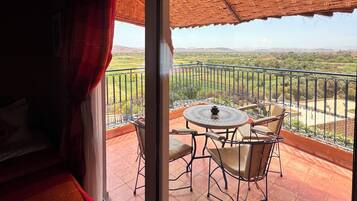 Quarto com varanda, mesa e cadeiras, vista para paisagem e teto com padrão.