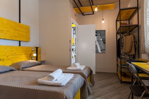 Quarto de hotel com duas camas, uma escrivaninha e um guarda-roupa.