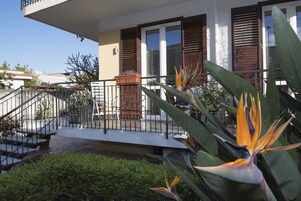 Um edifício residencial com varanda, escadaria e plantas em vasos.