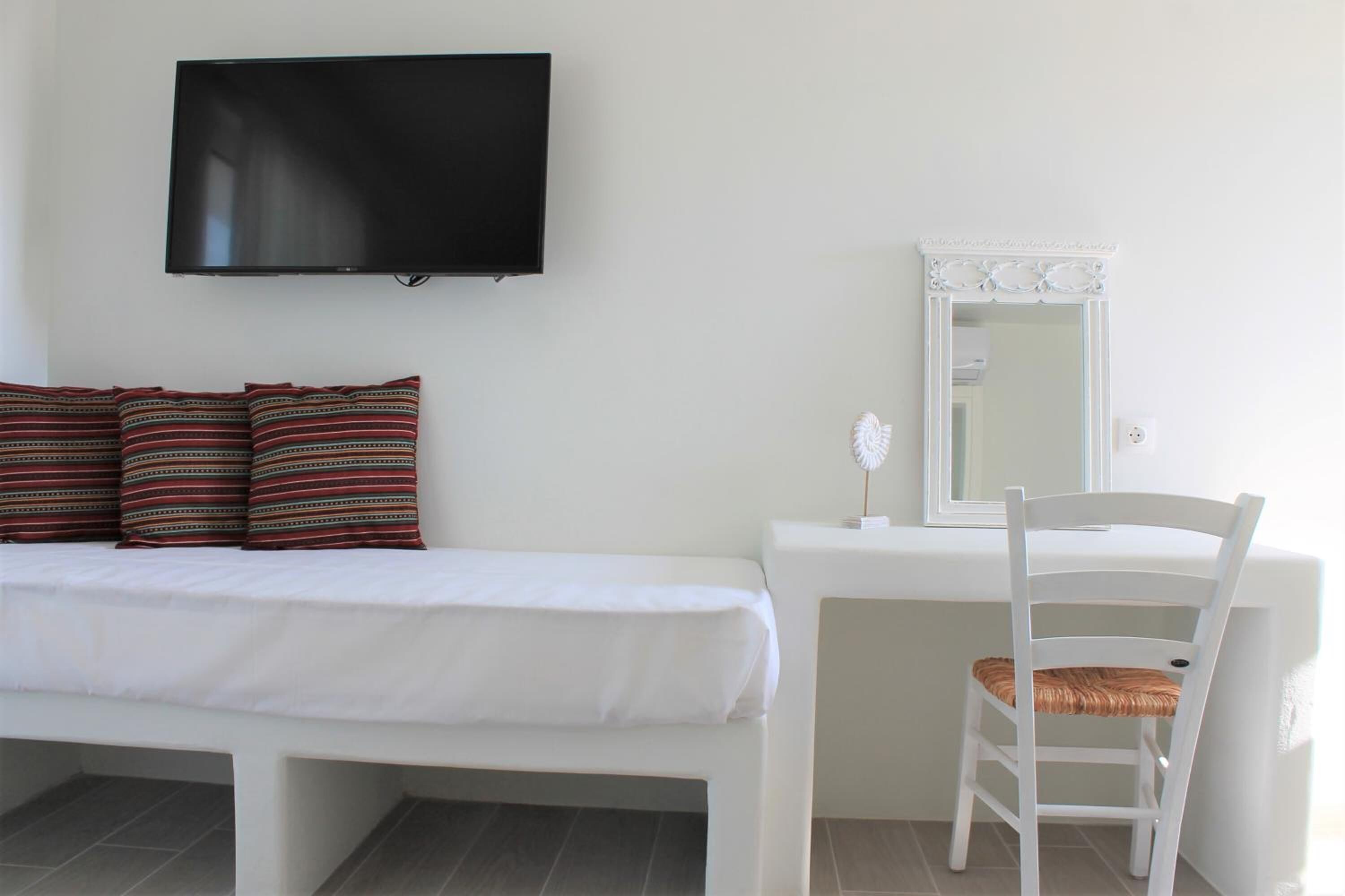 Quarto com cama, televisão na parede, uma cadeira e um espelho.