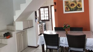 Uma sala de jantar com uma mesa posta para quatro pessoas, uma escadaria e uma cozinha ao fundo.
