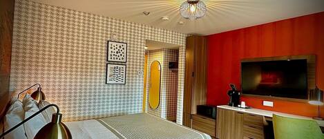 Um quarto com cama, escrivaninha, cadeira, televisão e luminária no teto.