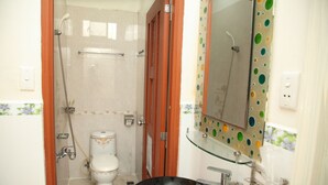 Casa de banho com sanita, chuveiro e uma pia de vidro com espelho estampado.