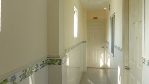 Um corredor estreito com paredes brancas, chão de azulejos e uma porta no final.