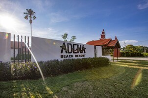 Placa para 'Adena Beach Resort', com céu claro e palmeiras.