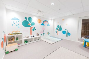 Quarto ideal para crianças, com espaço de recreação, prateleira branca cheia de brinquedos e uma janela grande.