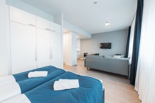 Quarto de hotel moderno com duas camas, um sofá cinzento e uma televisão de tela plana.