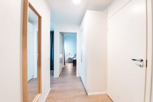 Um corredor estreito com piso de madeira que leva a um quarto com cama e escrivaninha.