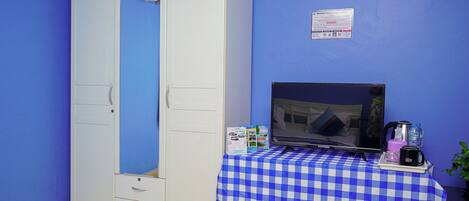Quarto com parede azul, guarda-roupa branco com duas portas, televisão sobre uma mesa e toalha de mesa xadrez.